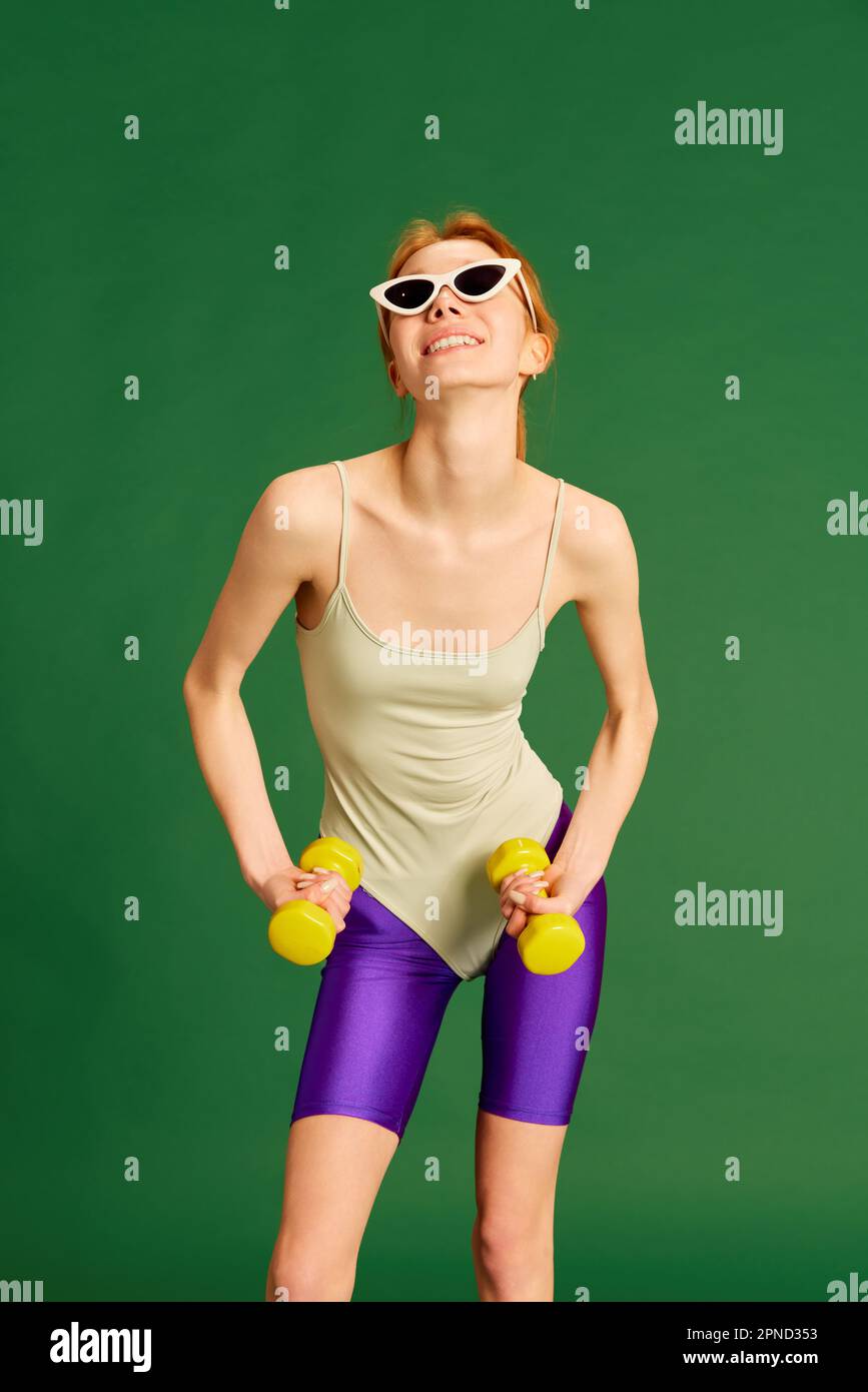 Sporty red haired young girl wearing sportswear training with dumbbells ...