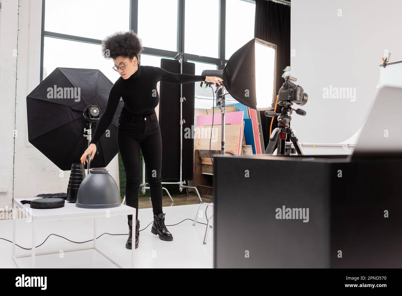 african american content producer in black clothes reaching lamps near ...