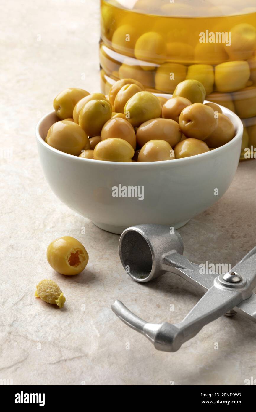 Bowl with green Turkish olives close up and a metal olive pitter and ...