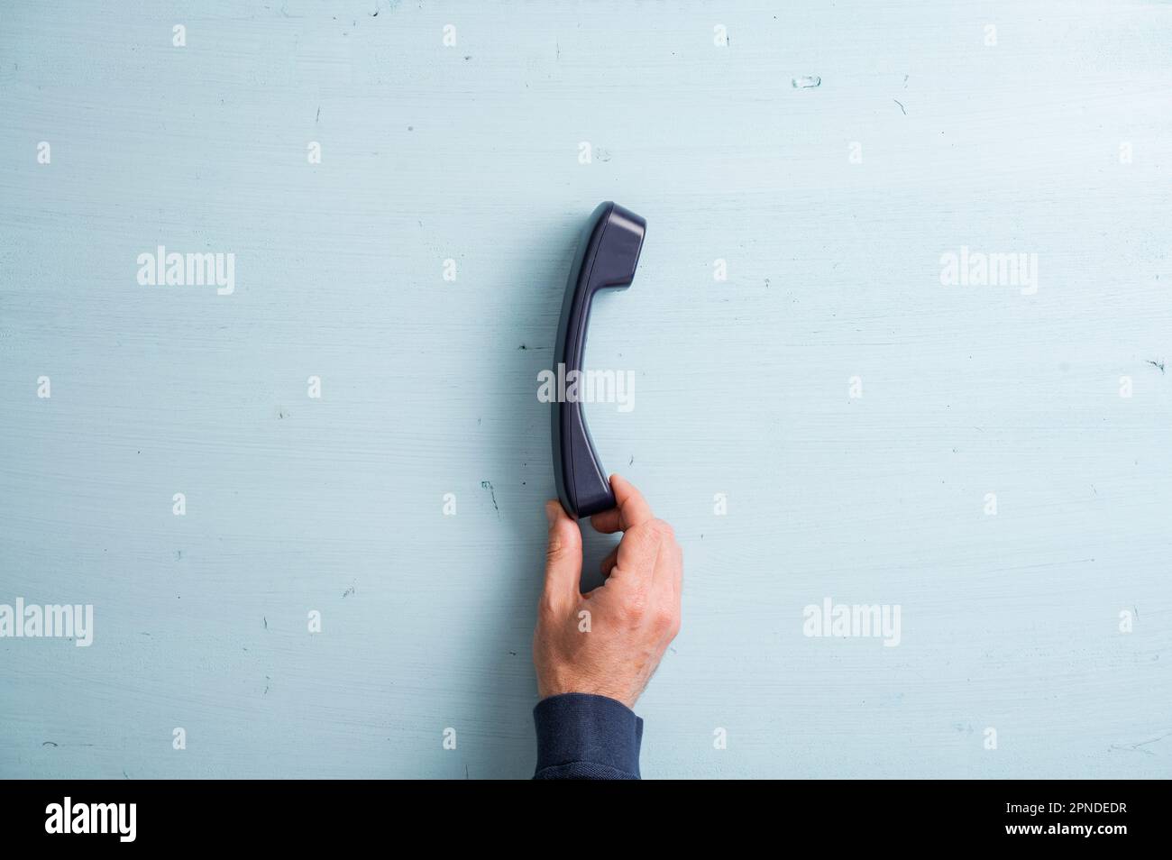 Male hand holding a black landline telephone handset. Over light blue ...