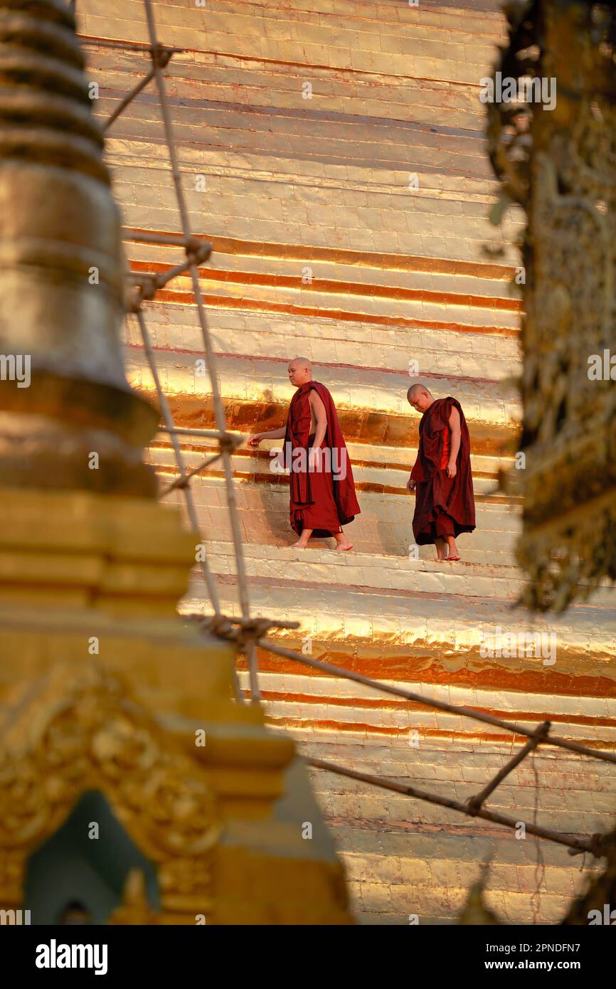 Two Buddhist monks walk on the golden stupa of the Shwedagon Pagoda ...