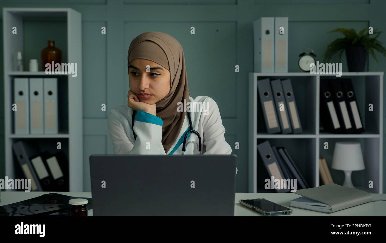 Thoughtful sad bored young therapist doctor woman sitting at clinic ...