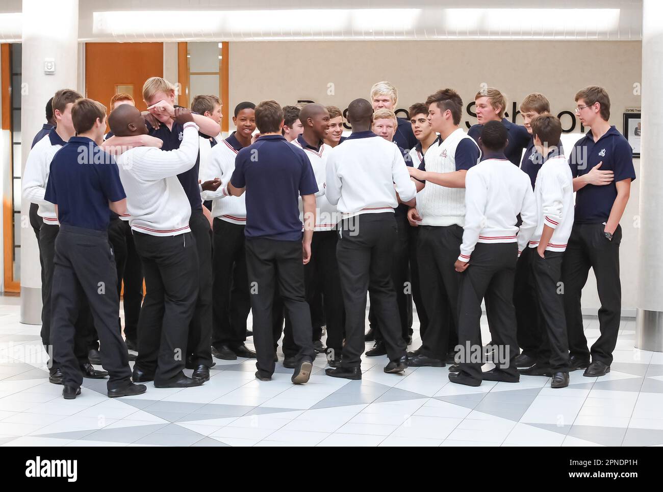A group of young diverse males in uniform huddled together at school ...