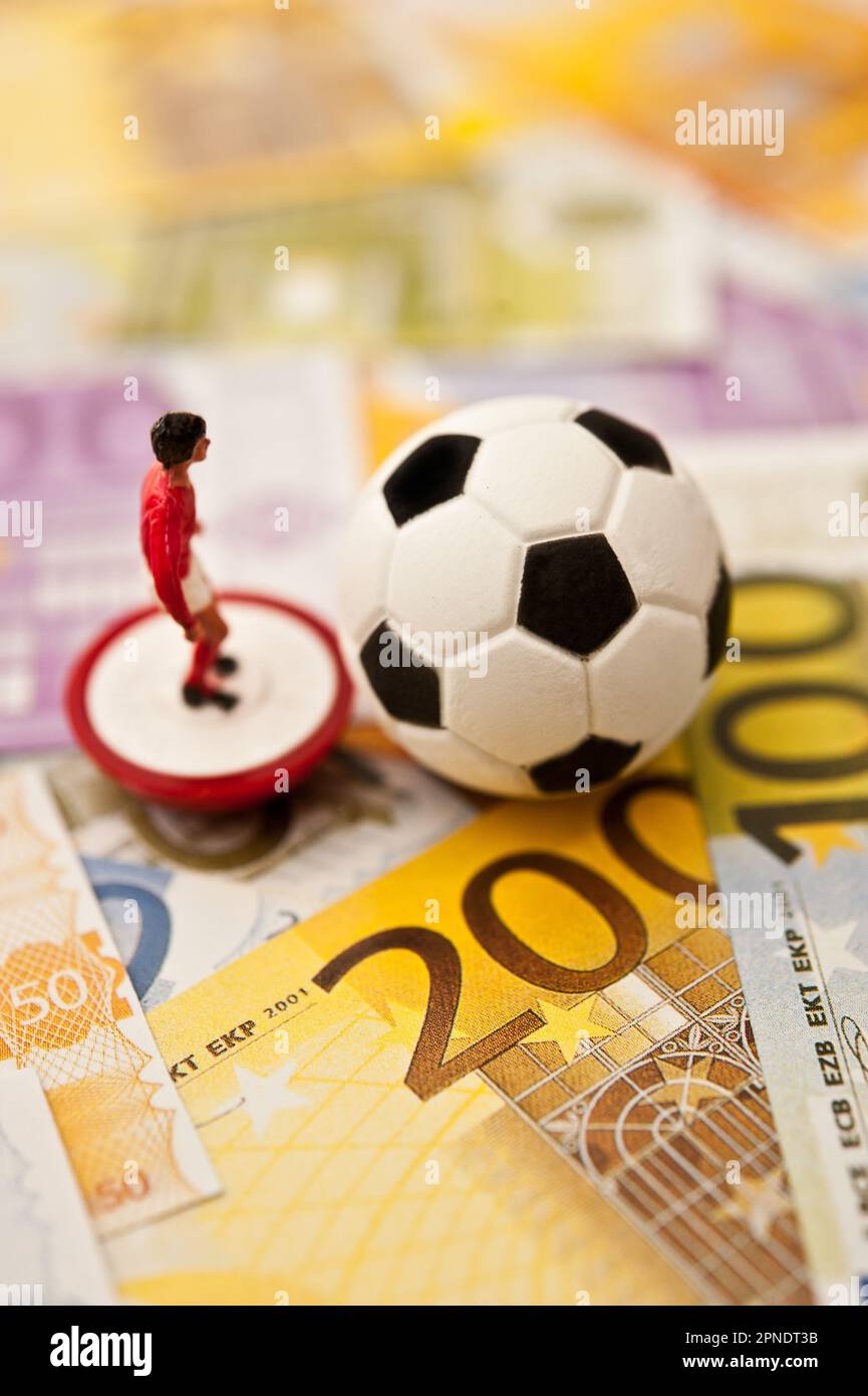 soccer ball and football player figurine over a background of money ...