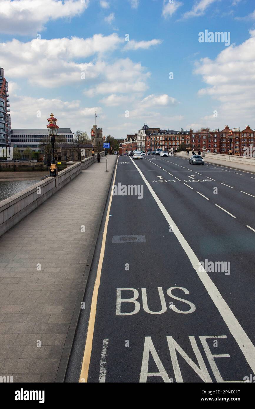 Bus lane on road crossing Putney Bridge, West London, under blue sky, with little traffic; high ...