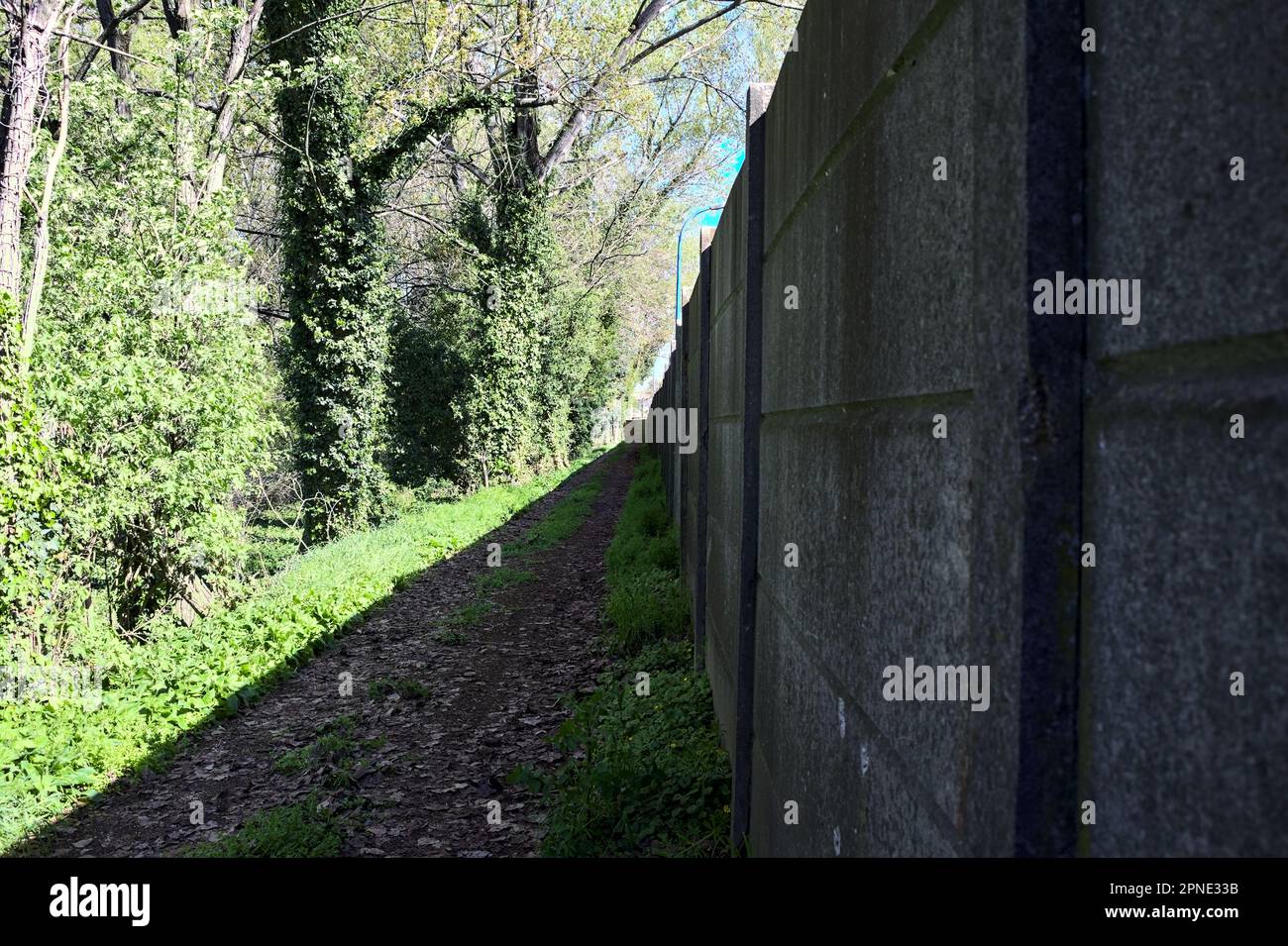 Path bordered by a concrete boundary wall of an industrial complex in a ...