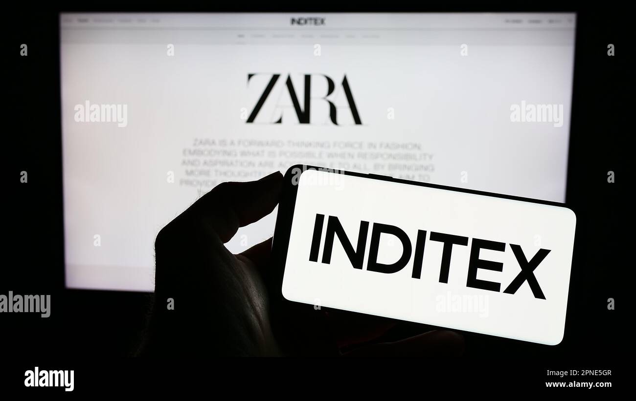Person holding mobile phone with logo of Industria de Diseno Textil S.A. (Inditex) on screen in ...