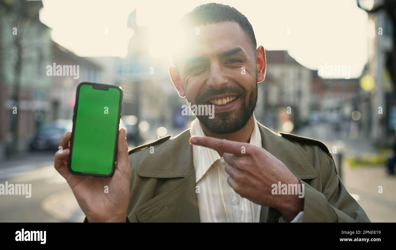 One cheerful Arab guy pointing at phone with greenscreen in chroma key ...
