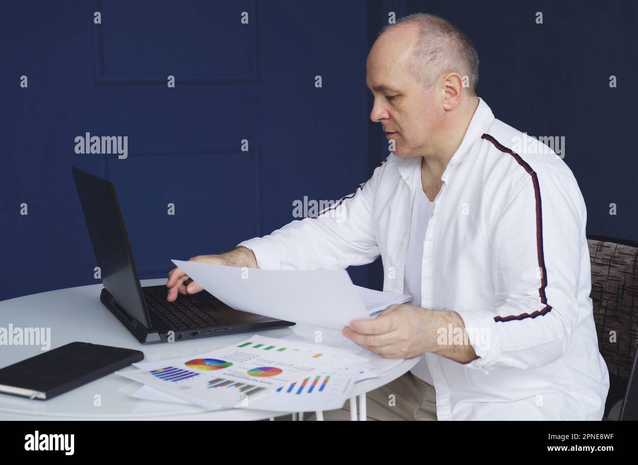 A male businessman works on a laptop, studies reporting documents ...