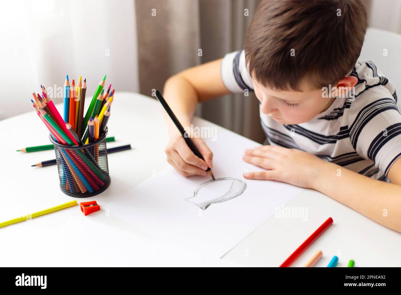 A child boy draws on white paper with colored pencils while sitting at ...