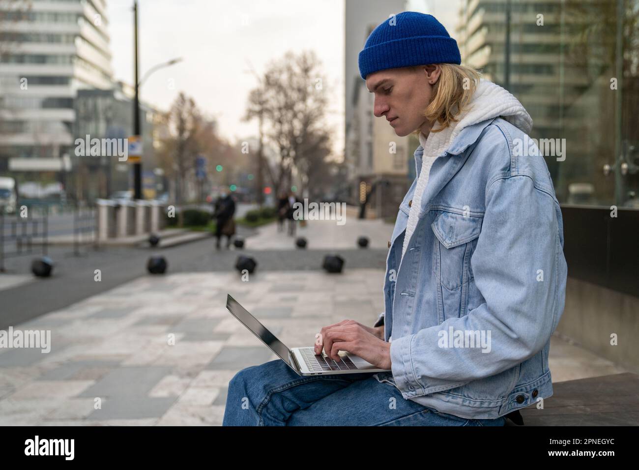 Focused guy freelancer doing urgent work on laptop on street sitting on ...