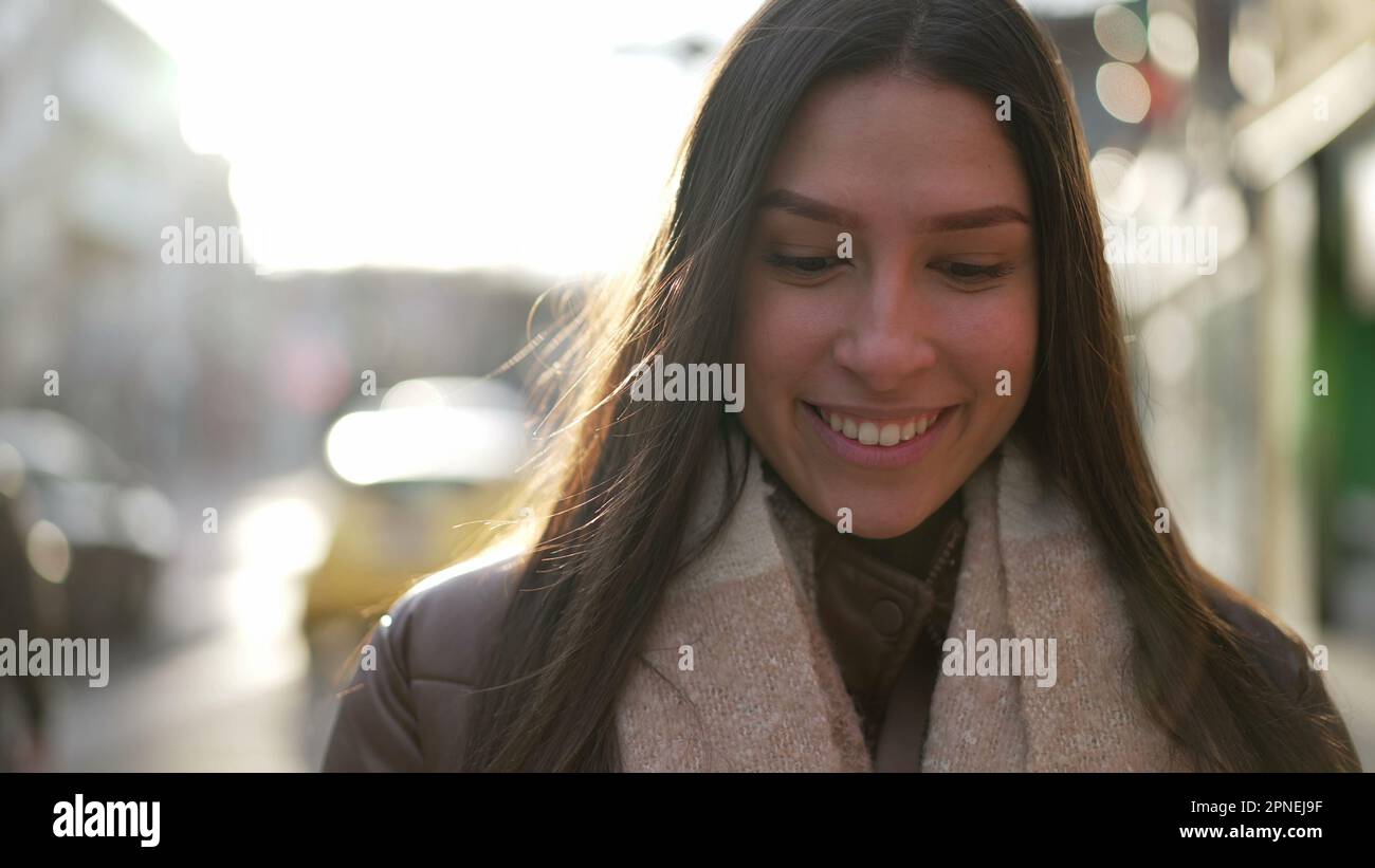 Portrait of a happy young woman walking toward camera outside in city ...