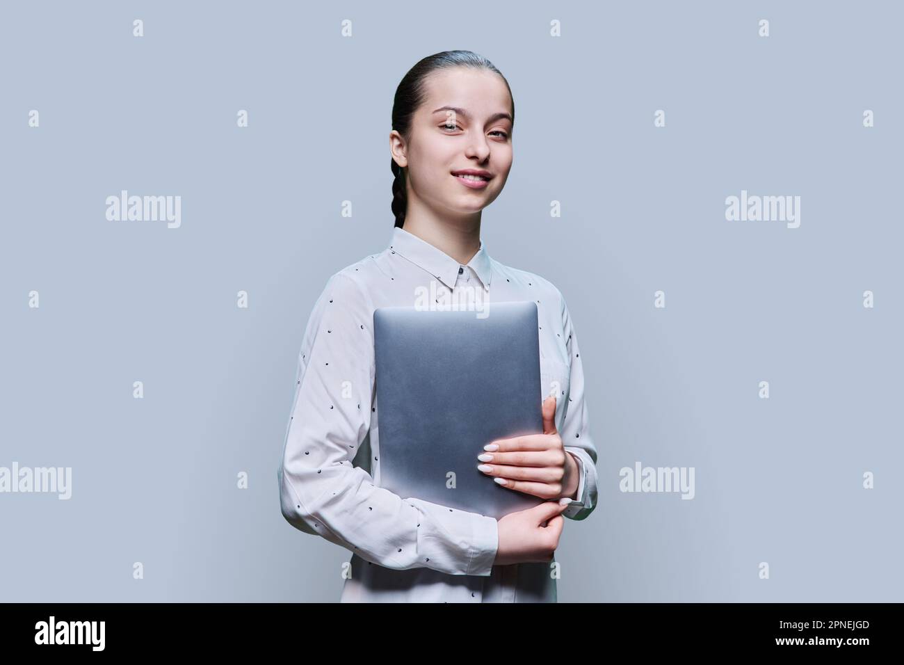 Teenage girl holding closed laptop in her hands, on grey studio ...