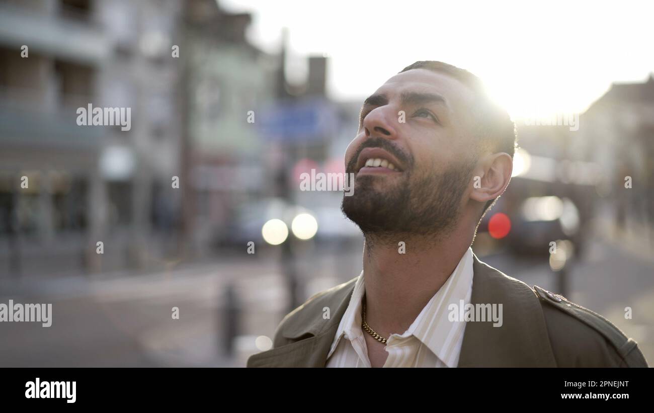 One thoughtful Middle Eastern young man standing in street looks up at ...