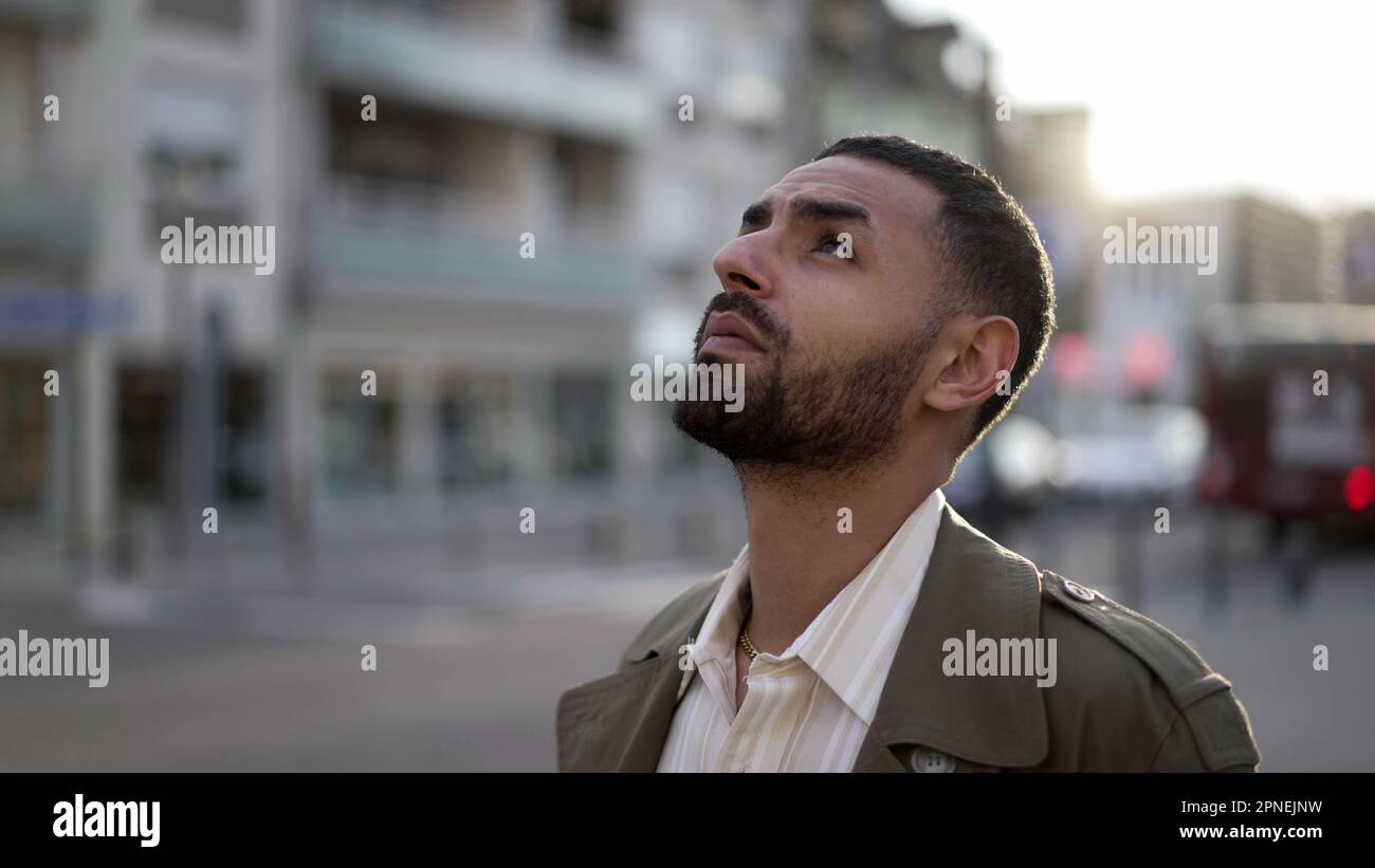 One thoughtful Middle Eastern young man standing in street looks up at ...