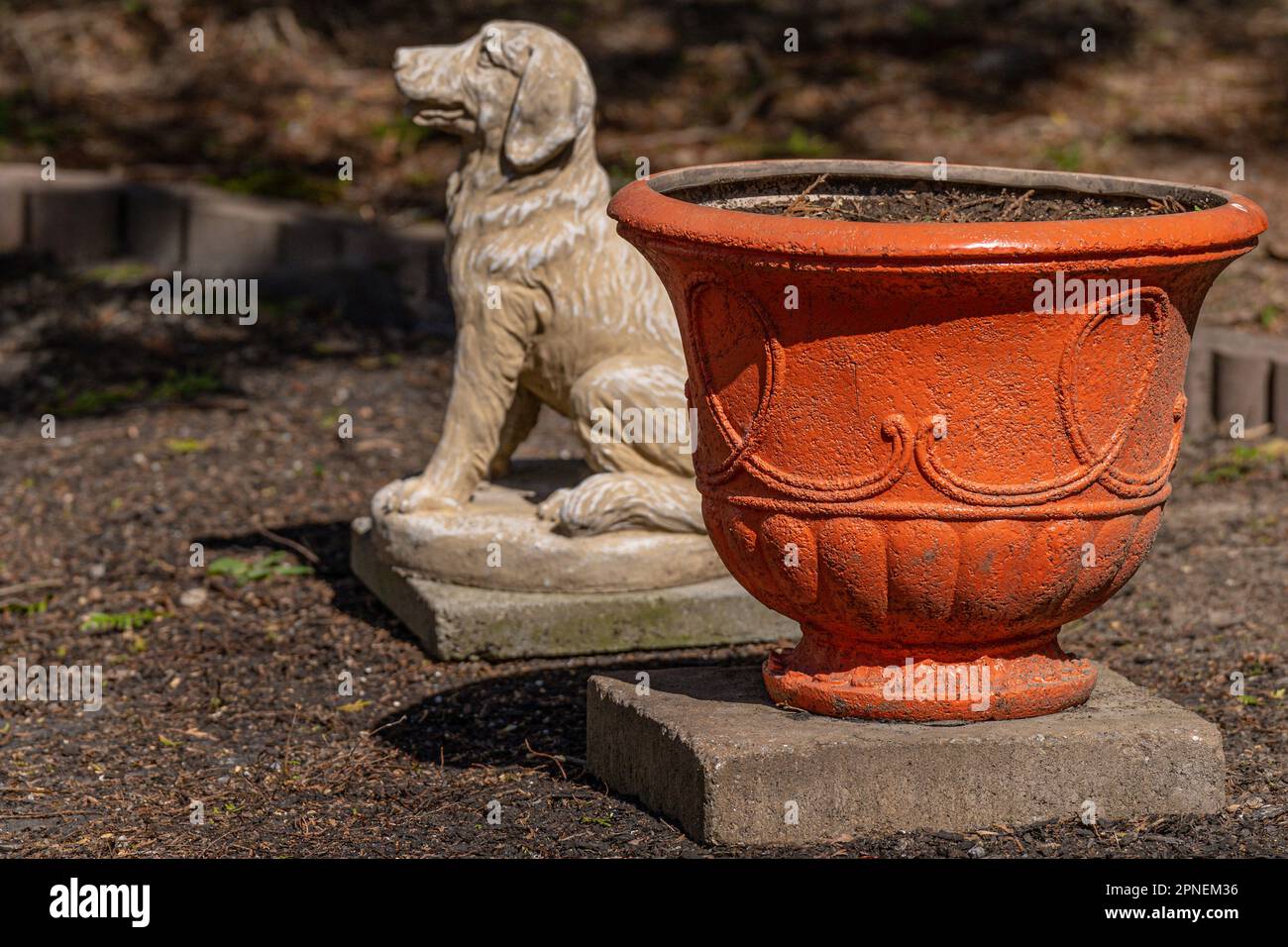 An orange concrete pot in focus in front of a slightly out of focus ...