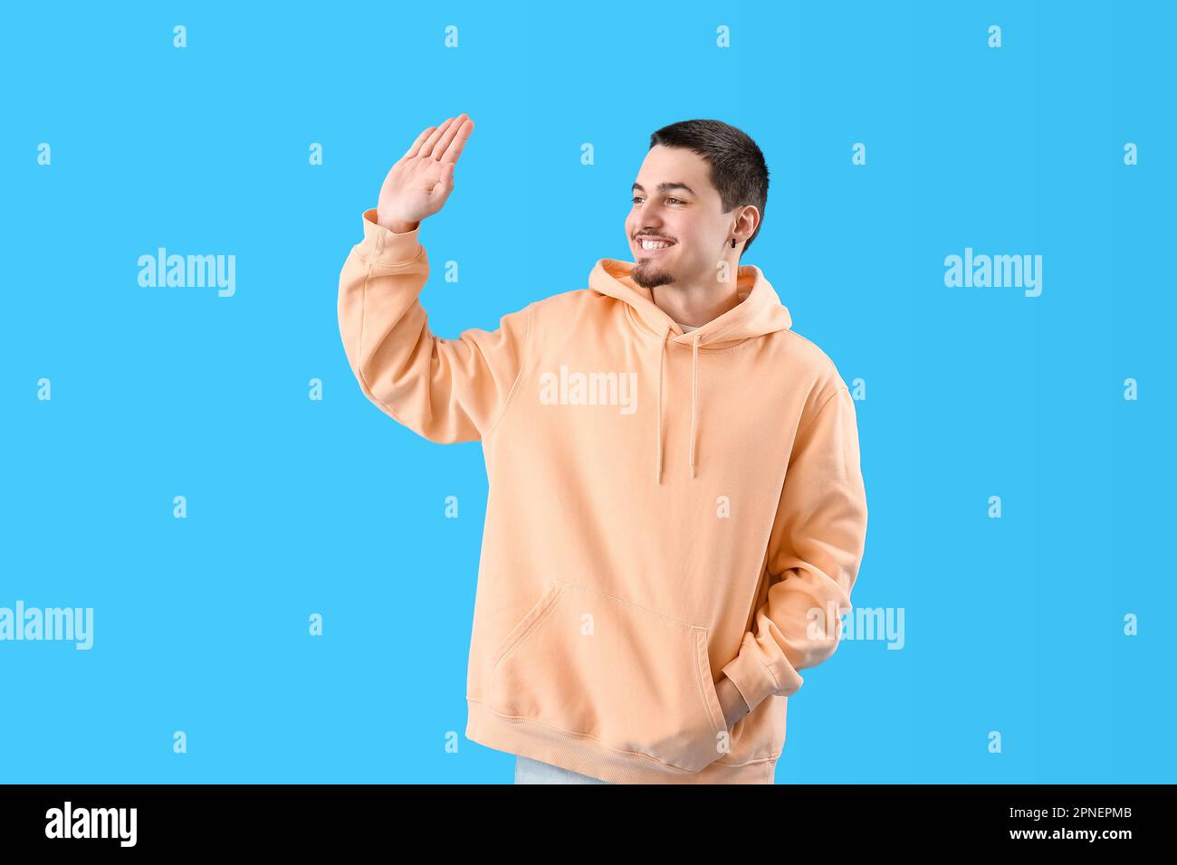Handsome young man in hoodie waving hand on light blue background Stock ...