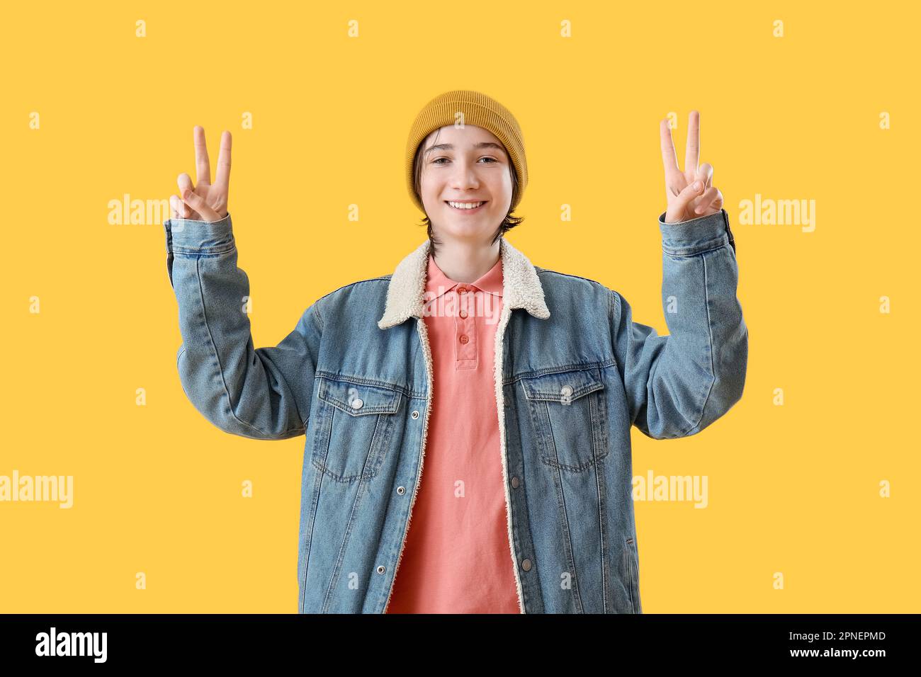 Teenage boy showing victory gesture on yellow background. Hello concept ...