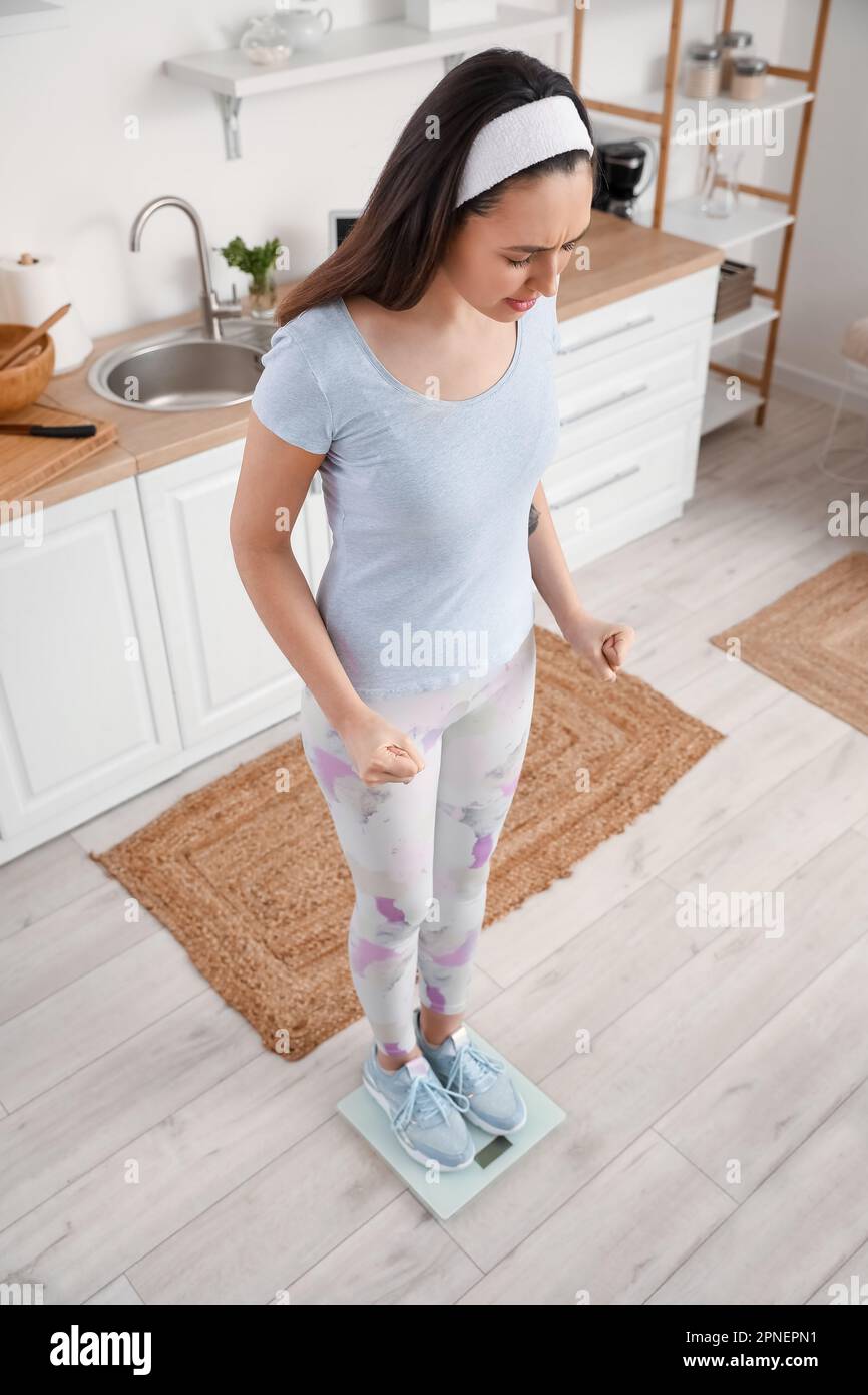 Sporty young woman measuring her weight on scales in kitchen Stock ...