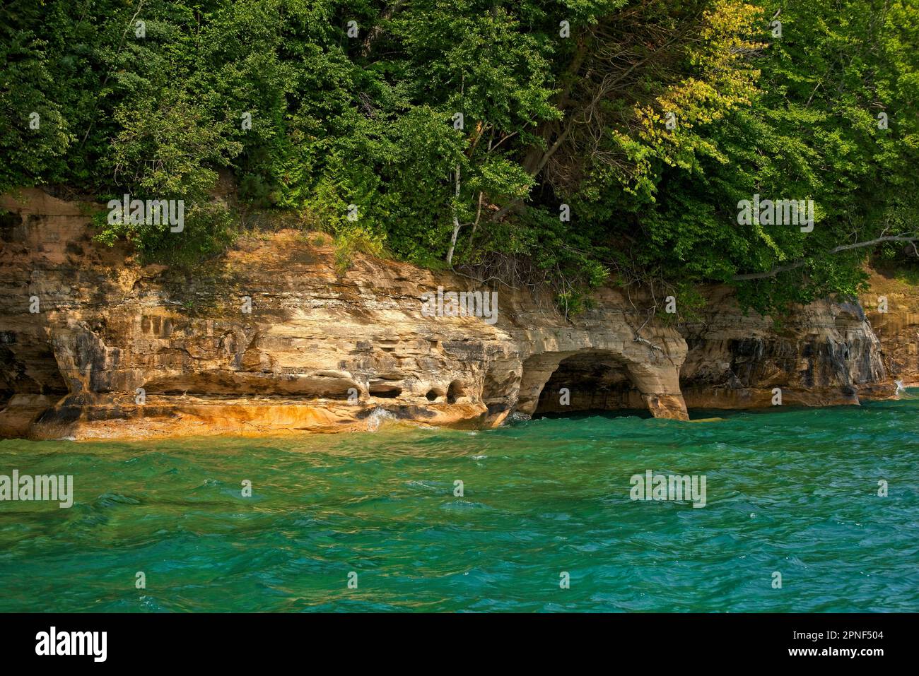 Wave-carved caves and stone arch at the base of cliffs on Grand Island ...
