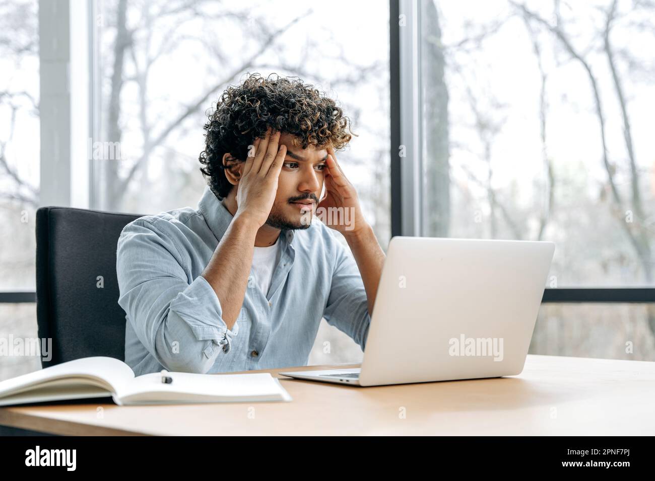 Sad worried indian or arabian curly man, financial manager, company ceo, sitting at a desk in ...