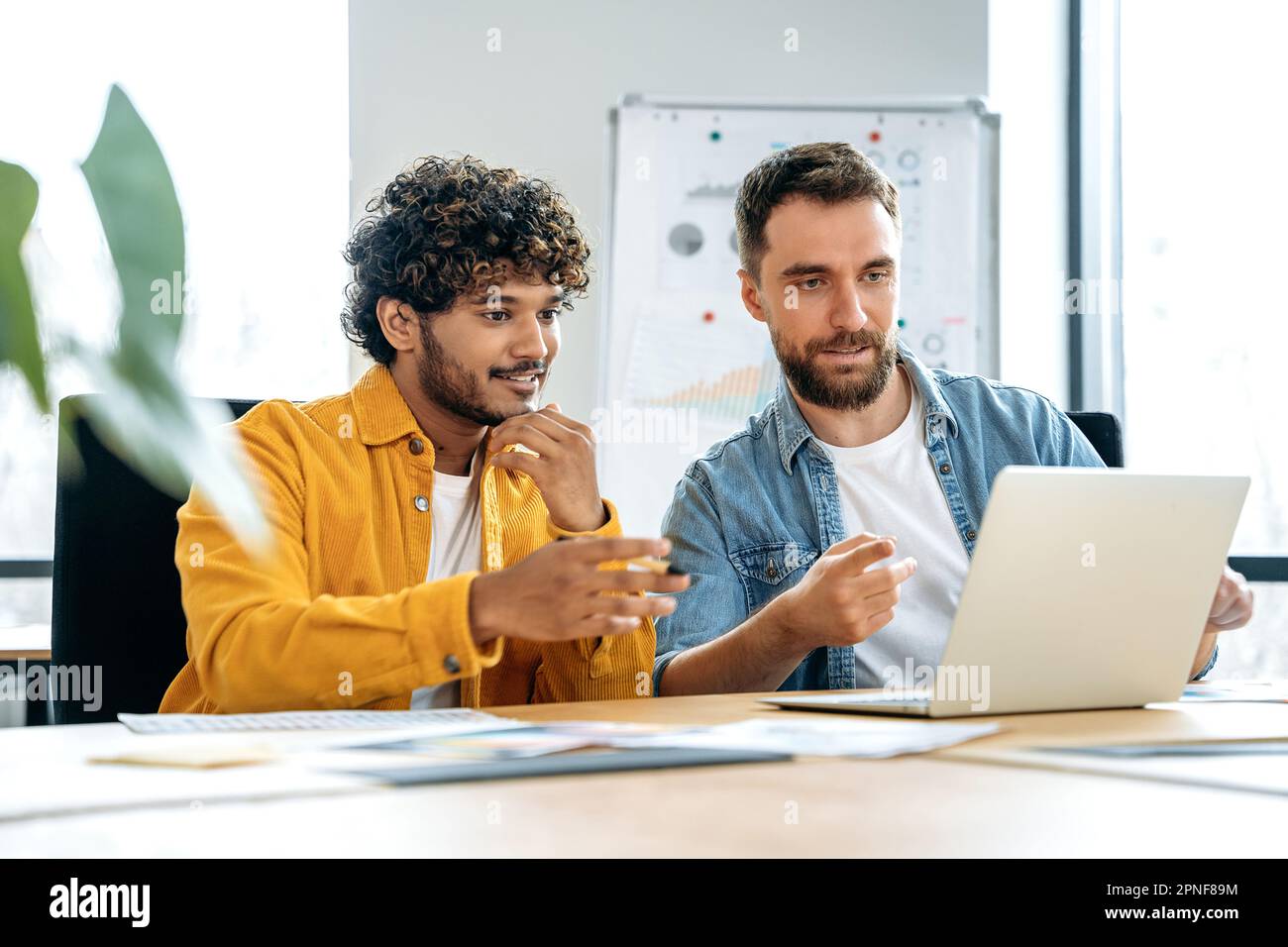 Two male multiracial professional employees sit in the office at the ...