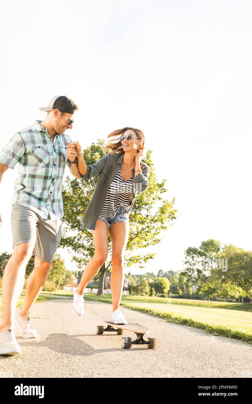 Man helping woman to balance while riding longboard Stock Photo - Alamy