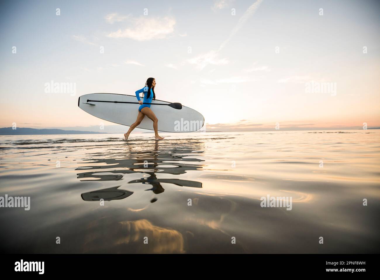 Woman running on beach with paddleboard at sunset Stock Photo - Alamy