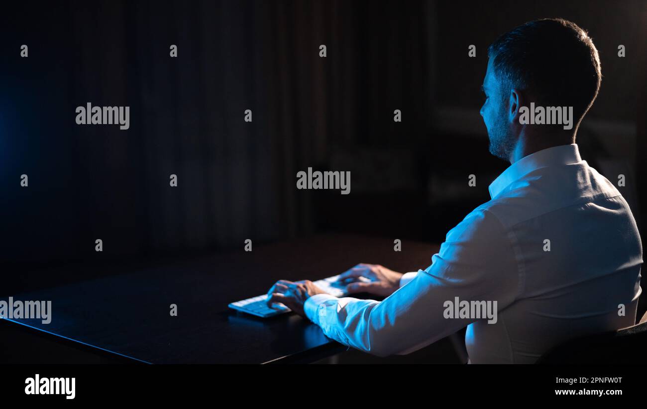 Rear view of a man typing on a keyboard in the dark Stock Photo - Alamy