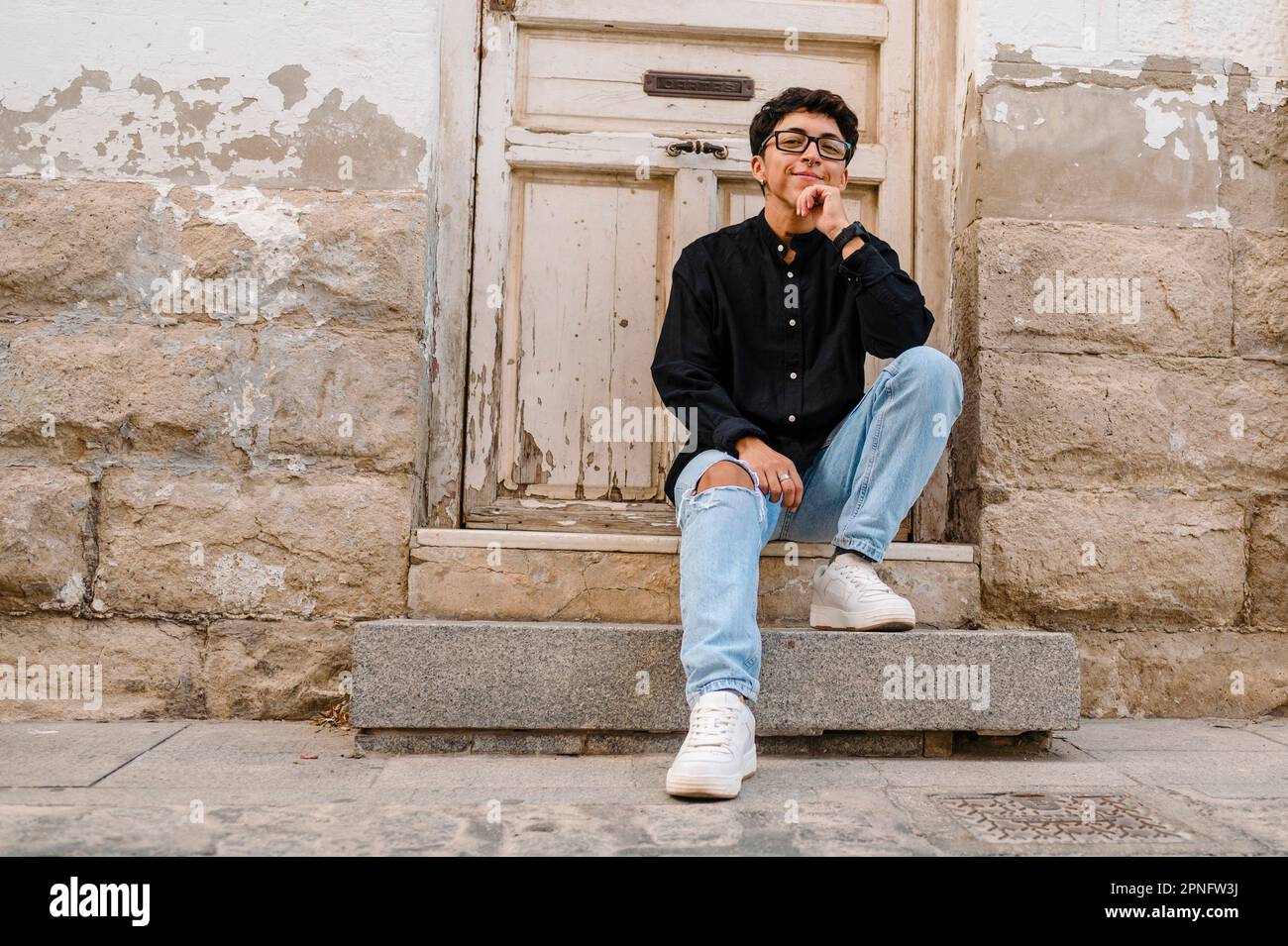 Young transgender man posing sitting on the front steps of a house ...