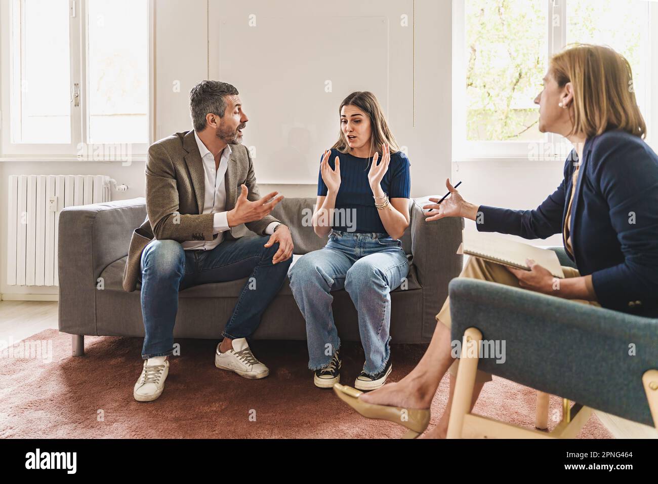 A married couple heatedly arguing on a couch during a family therapy ...