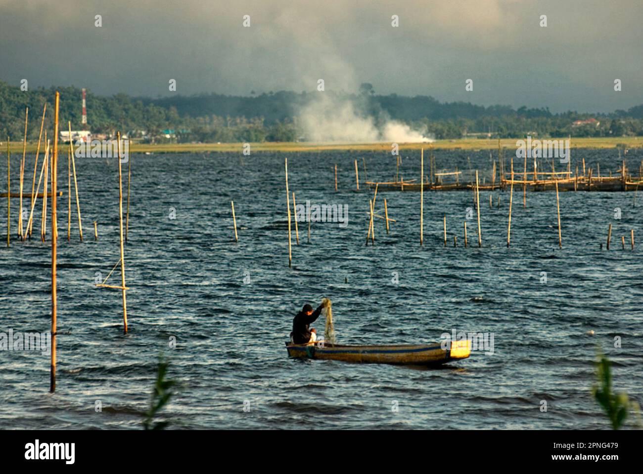 A fisherman is working from a boat, in a background of fish farming ...