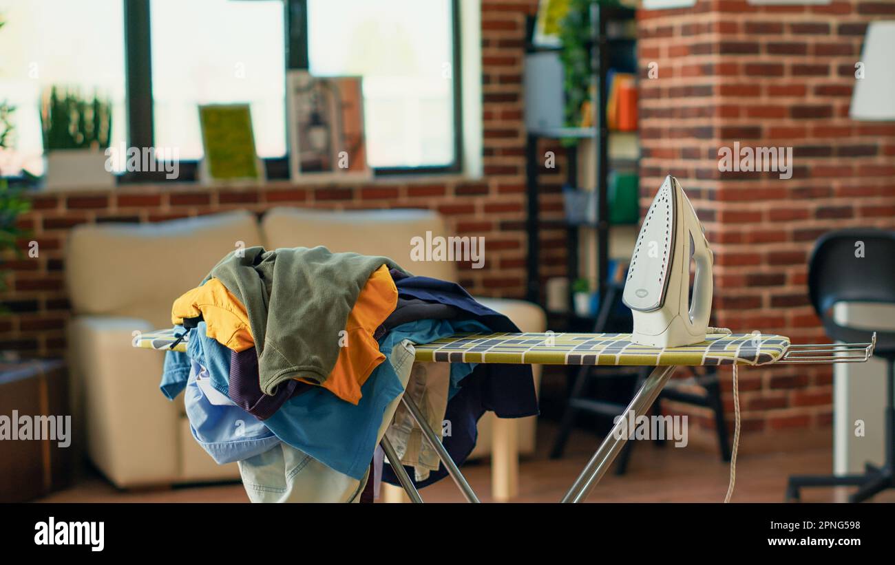 Empty living room with iron and ironing board, large pile of laundered ...