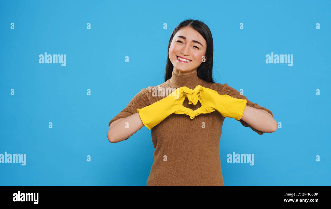 Happy asian maid wearing yellow gloves while doing heart shape in front ...