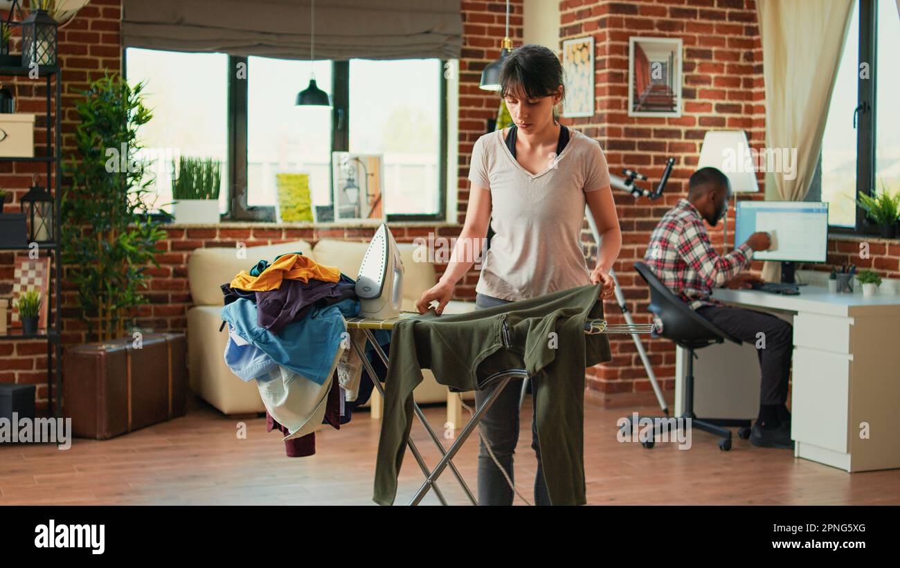 Female person ironing blouse in apartment after doing laundry, using ...