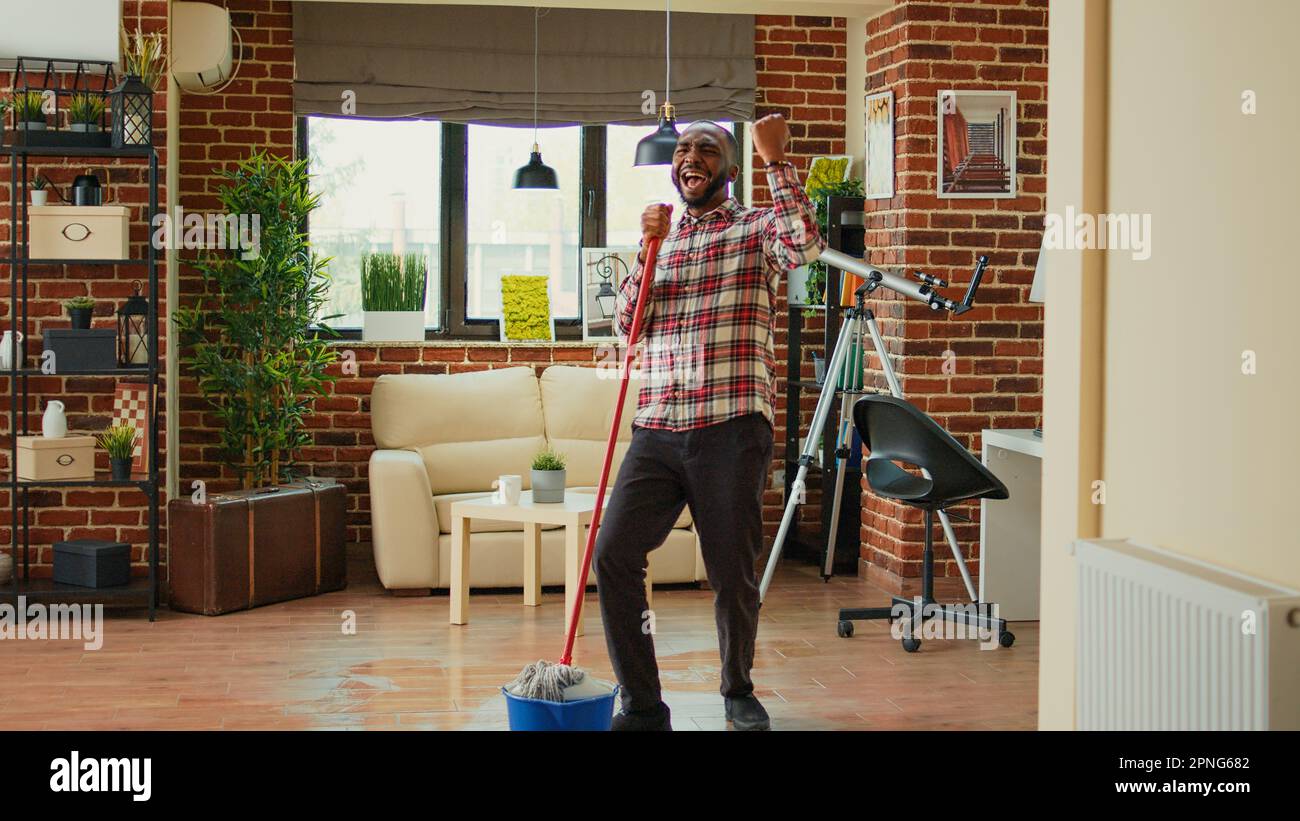 African american man mopping apartment floor to clean dust, using mop ...