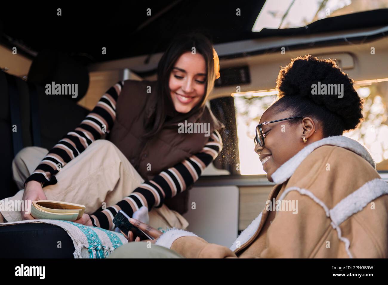 two young women chilling reading in camper van Stock Photo - Alamy