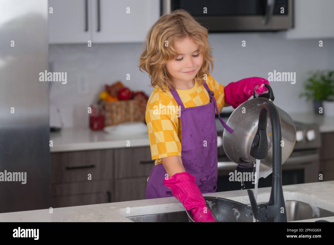 Kid washing dishes in the kitchen interior. Child helping with ...