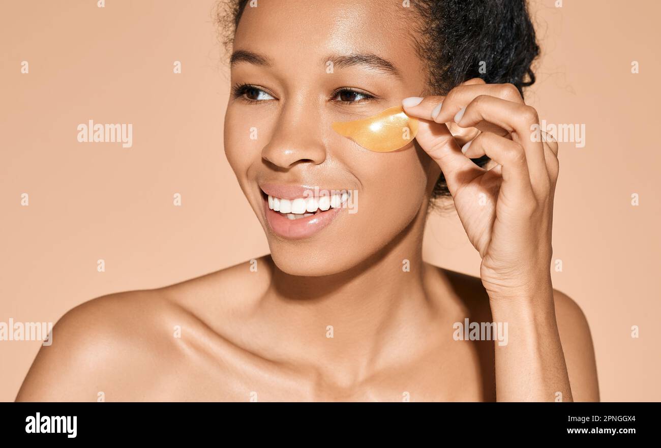 Curly swarthy woman applying under eye golden cosmetic patches ...