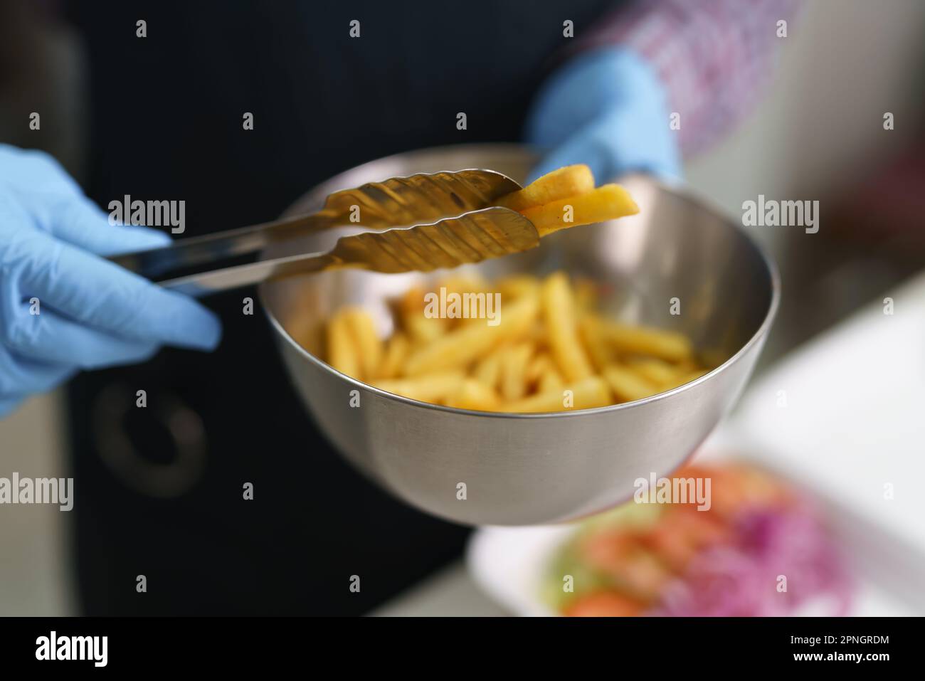 The cook serving fries with tongs. Fast food restaurant worker ...