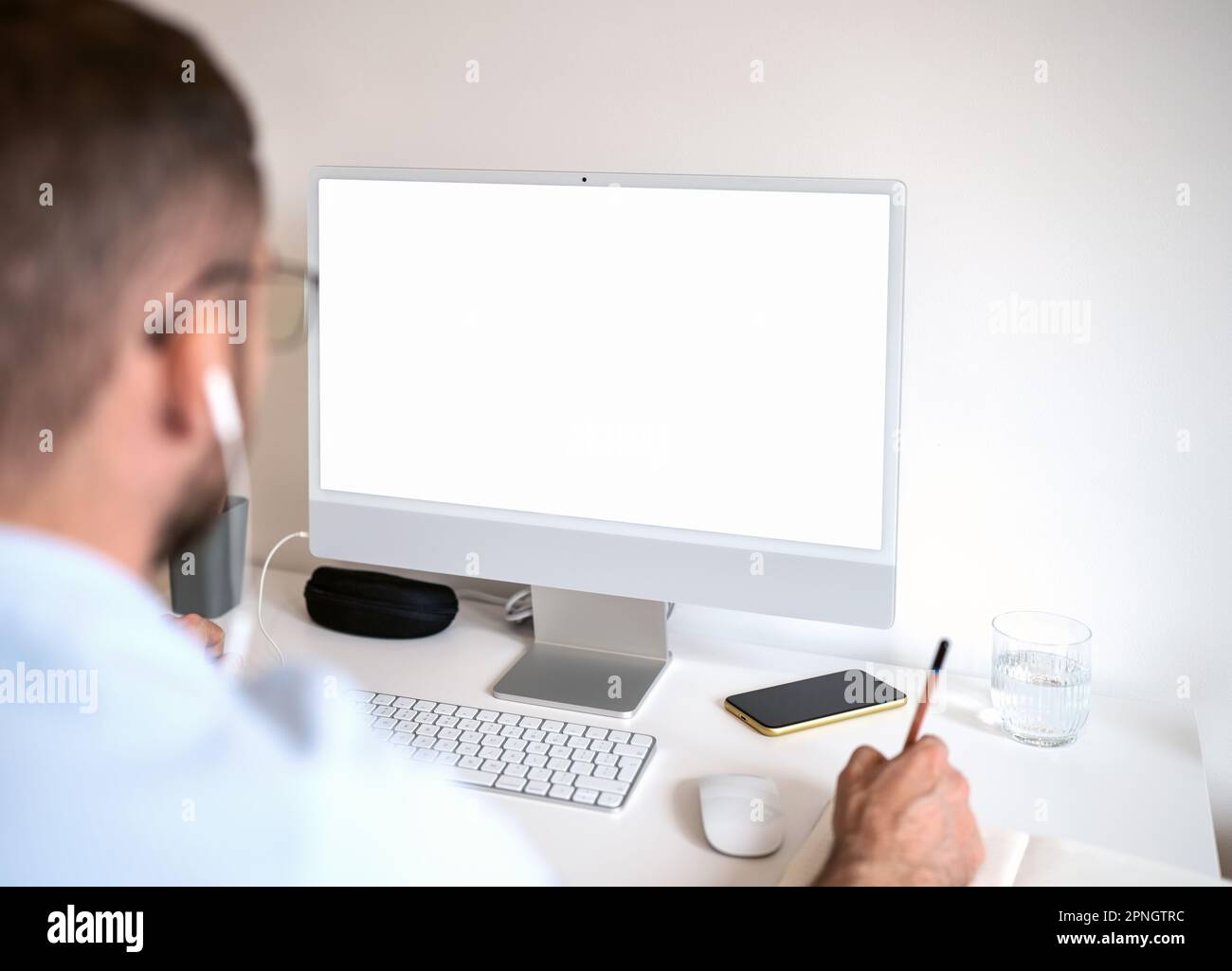 Male person sitting at desk looking at computer screen and writing ...