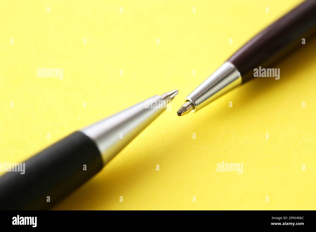 Two pens opposite each other on yellow paper background Stock Photo - Alamy