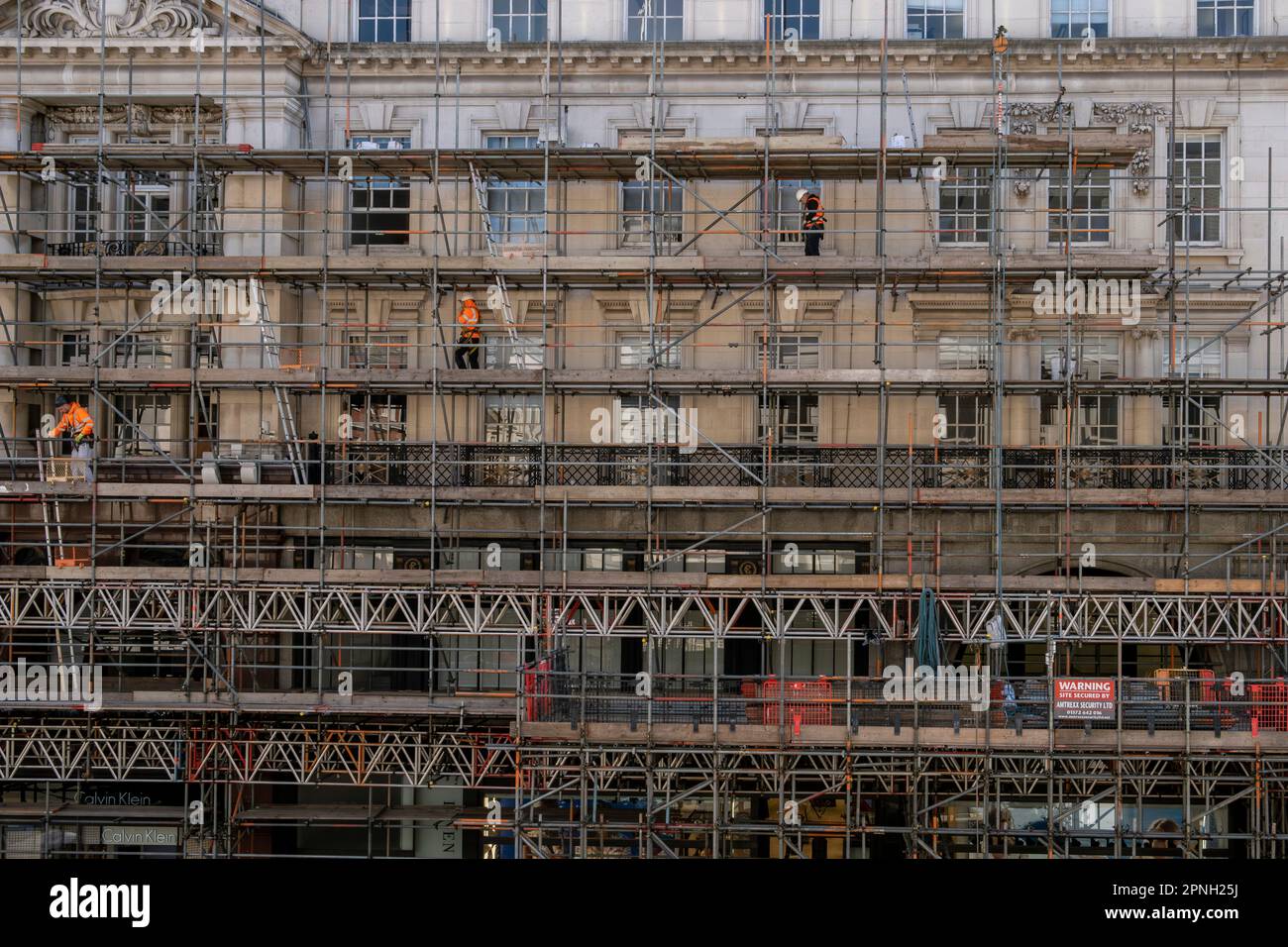 Scaffolders wearing fluorescent jackets and hard hats erect scaffolding ...