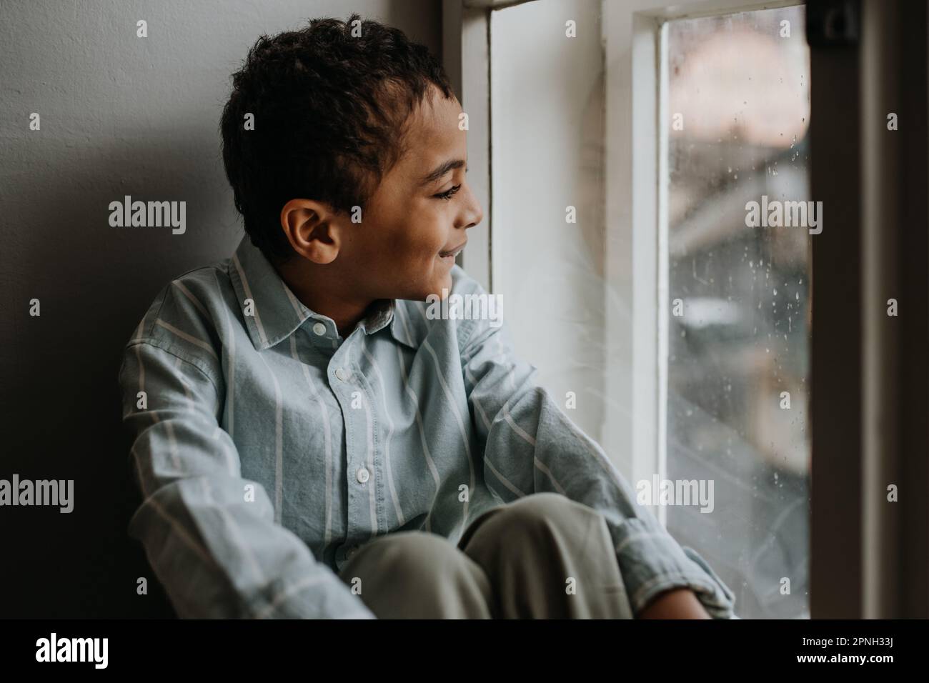 Little multiracial boy looking out of window Stock Photo - Alamy