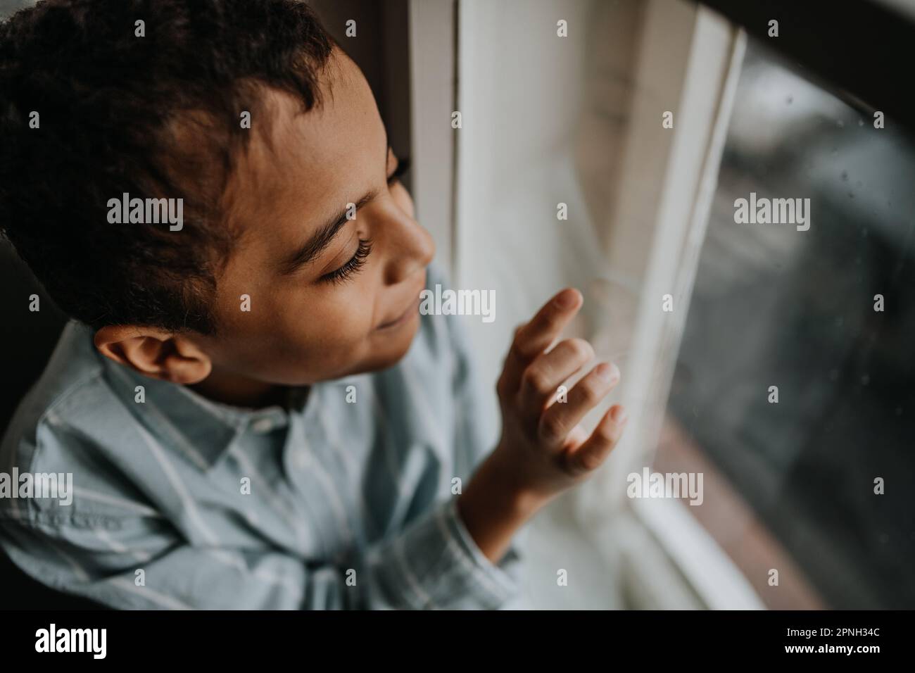 Little multiracial boy looking out of window Stock Photo - Alamy