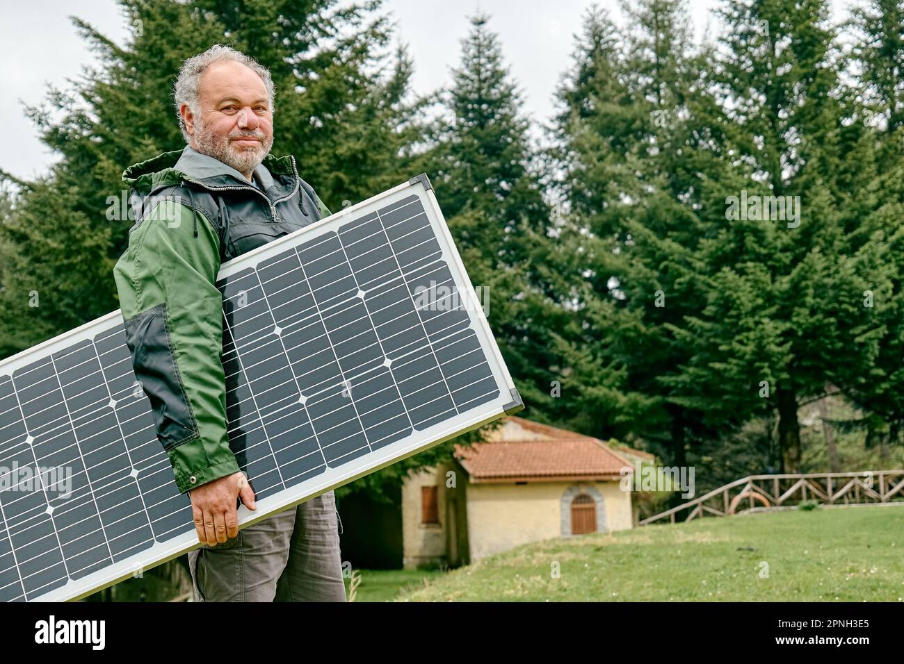 Middle aged bearded man carrying solar panel near house in rural zone ...