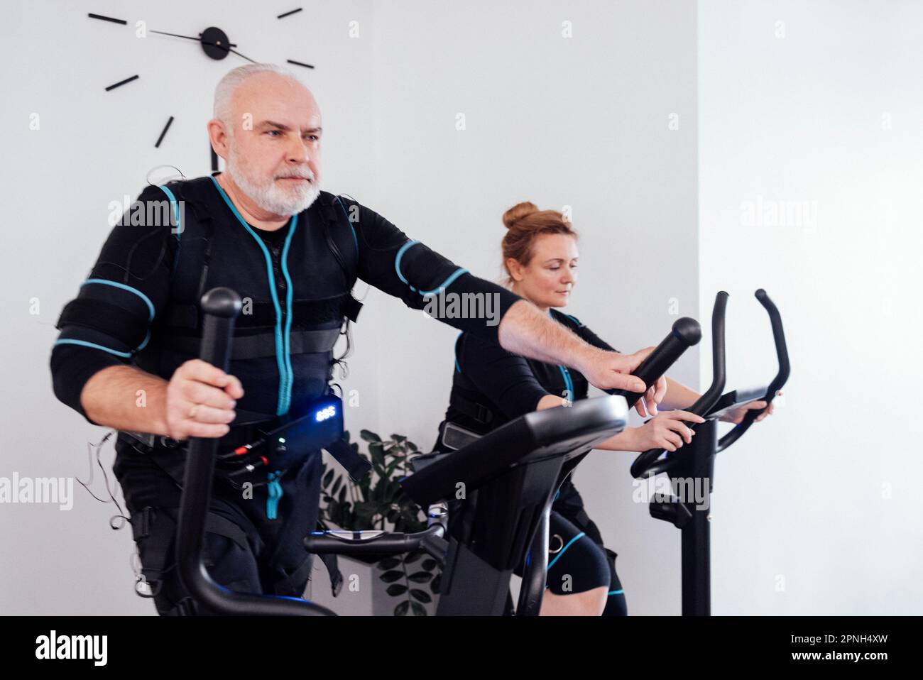 Couple of elderly people in ems suits are engaged in sports equipment ...