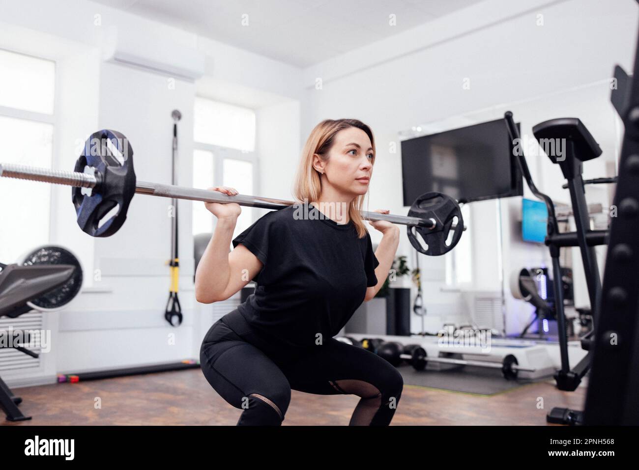 Strained pretty sportswoman in black sportswear lifting up bar. Young ...