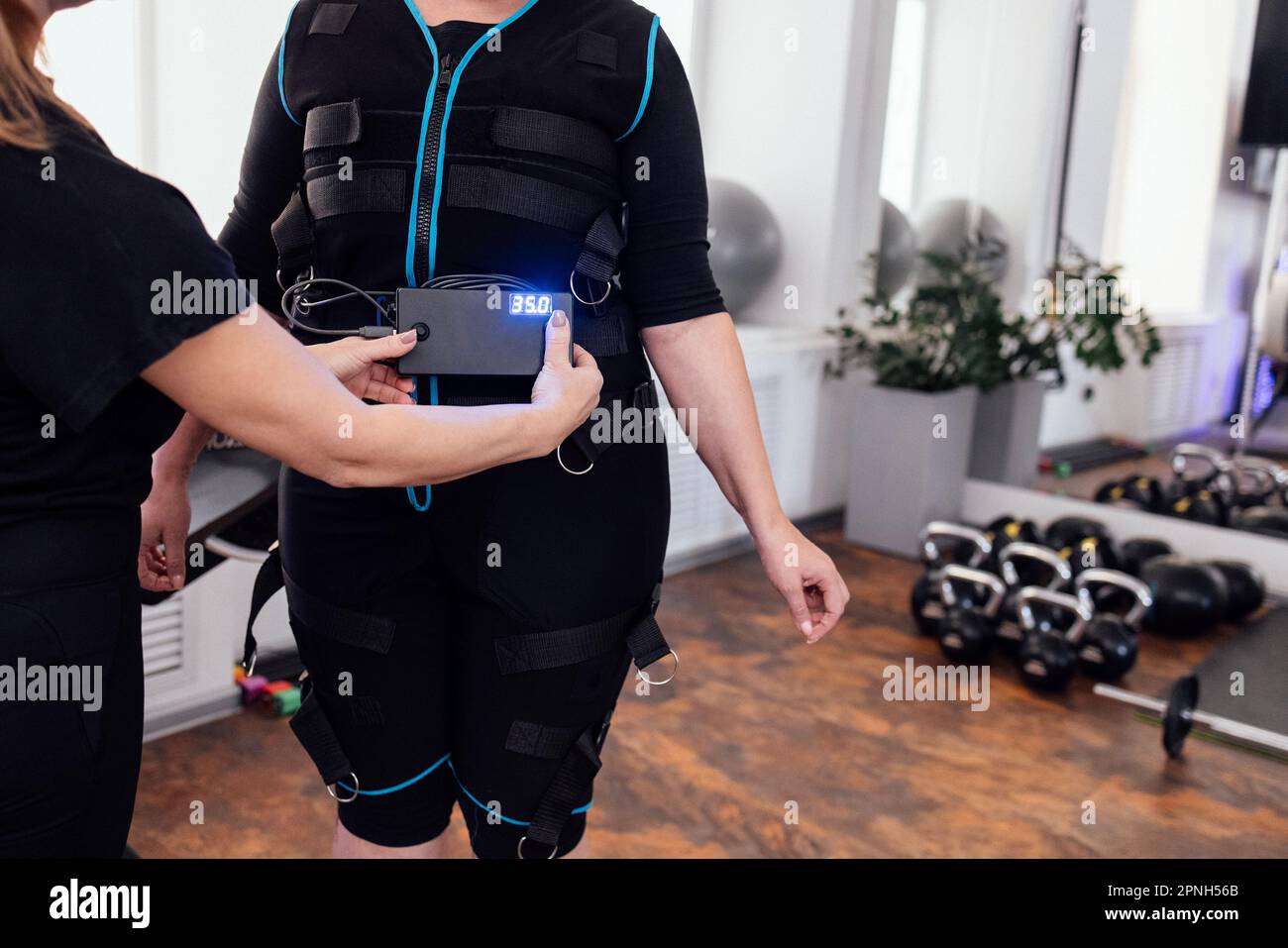 Close up of trainers hands help to put on ems suit to female plump ...