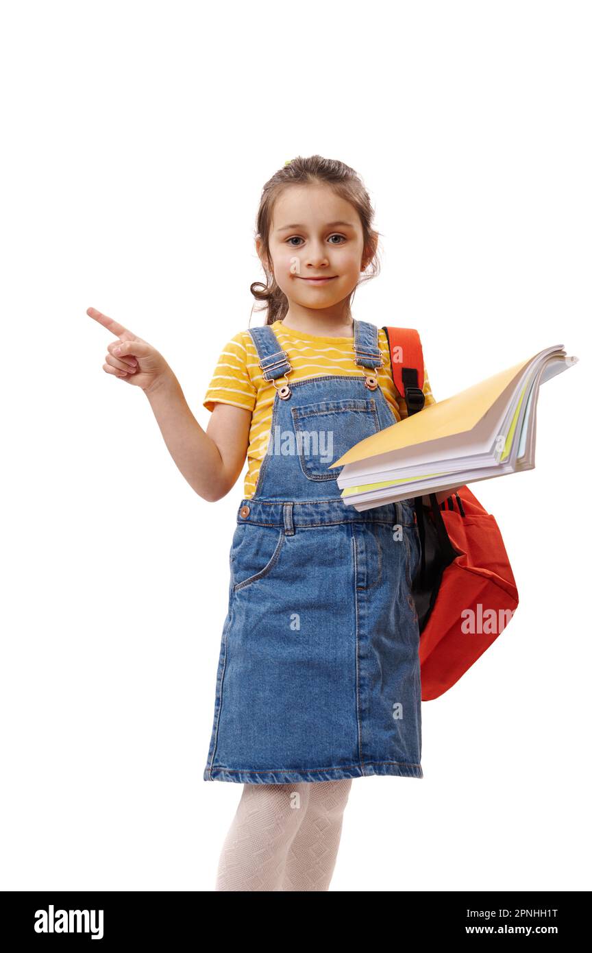 Schoolgirl, first grader holding books, pointing finger at copy space ...
